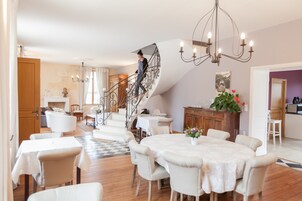 Uma sala de estar ampla com escada, mesas de jantar e um lustre.