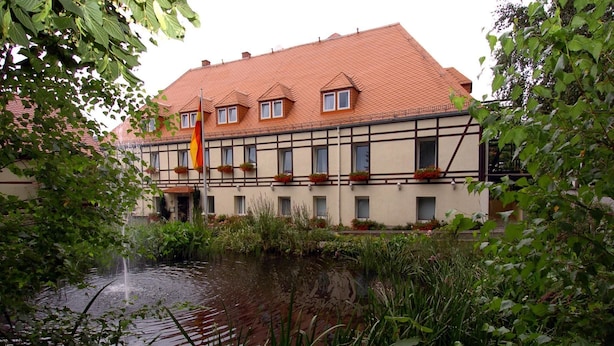Um edifício tradicional com telhado de cerâmica, várias janelas e um jardim com lago.