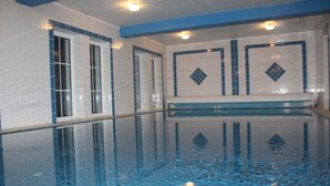 Uma grande piscina interior com água cristalina, paredes revestidas de azulejos e detalhes em azul.