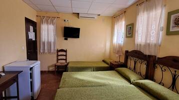 Quarto com duas camas, uma escrivaninha, uma cadeira, televisão e janela com cortinas.