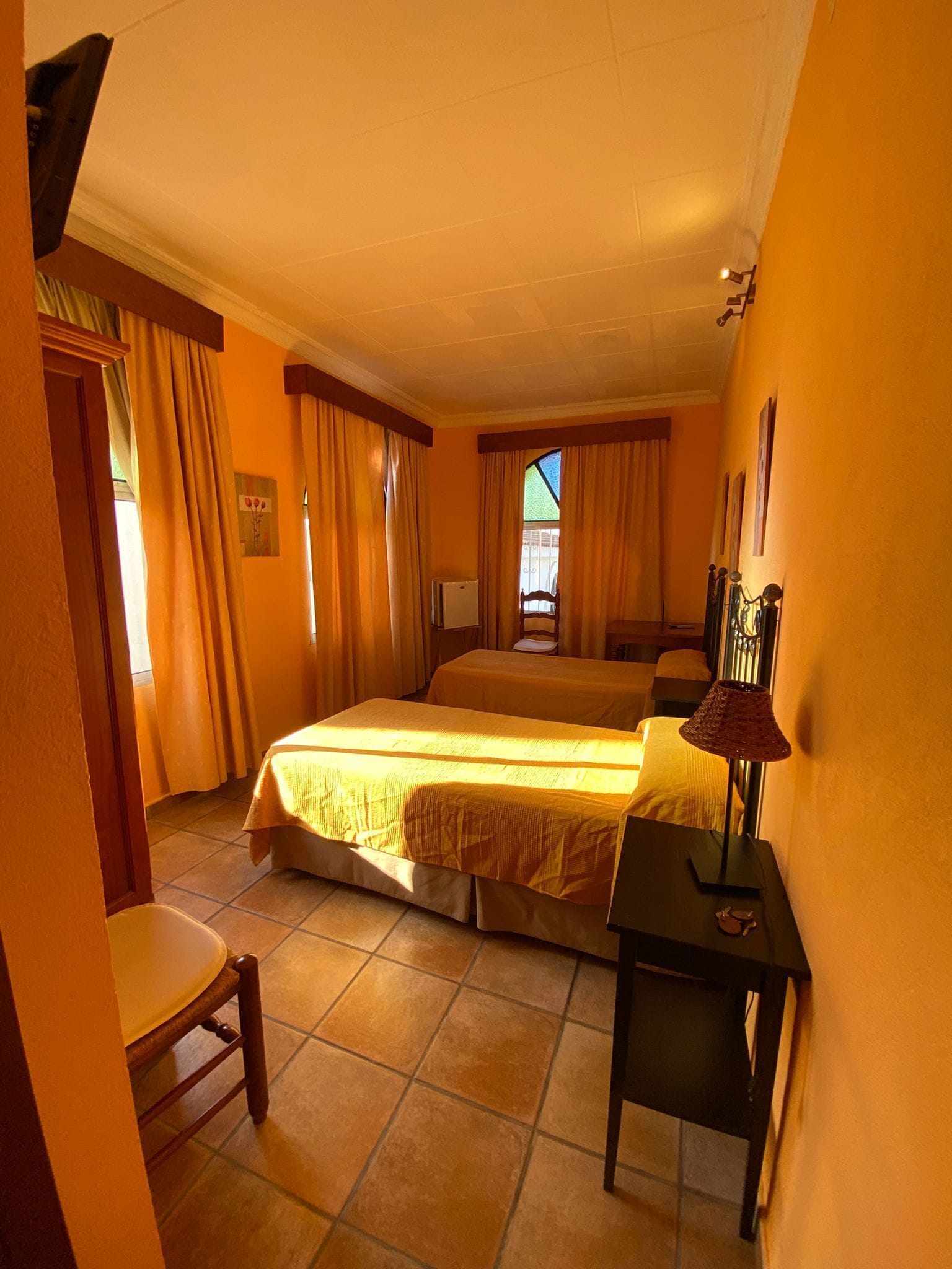 Quarto de hotel com duas camas, uma escrivaninha, uma cadeira e uma janela com cortinas.