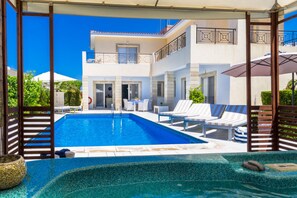 Uma área de piscina moderna com piscina azul cristalina, espreguiçadeiras e uma banheira de hidromassagem.