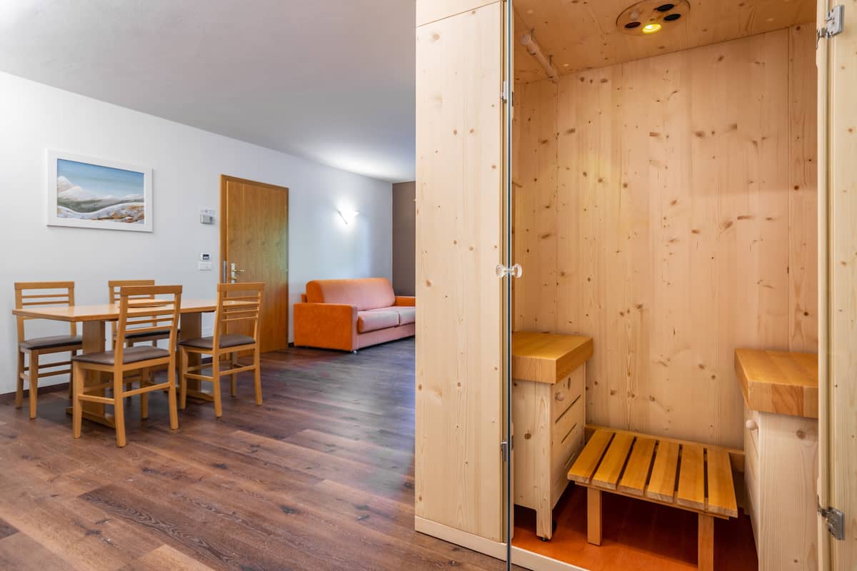Um quarto com piso de madeira, um banco de madeira, uma mesa de madeira com cadeiras, um sofá e um guarda-roupa de madeira.