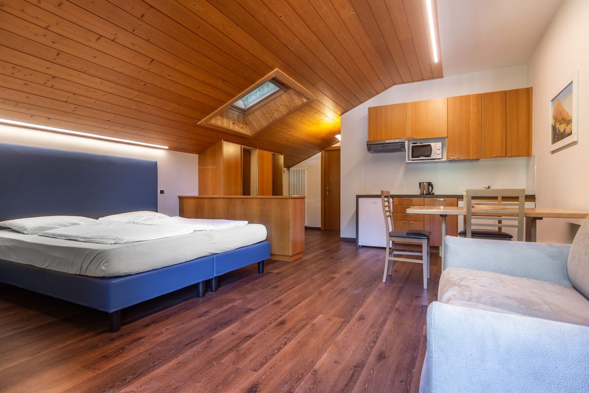 Quarto compacto com cama, escrivaninha e pequeno espaço de cozinha.