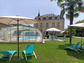 Piscina com cobertura de vidro, área de estar ao ar livre e um edifício grande ao fundo.