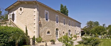 Um edifício de pedra com escadaria, janelas em arco e um jardim com plantas em vasos.