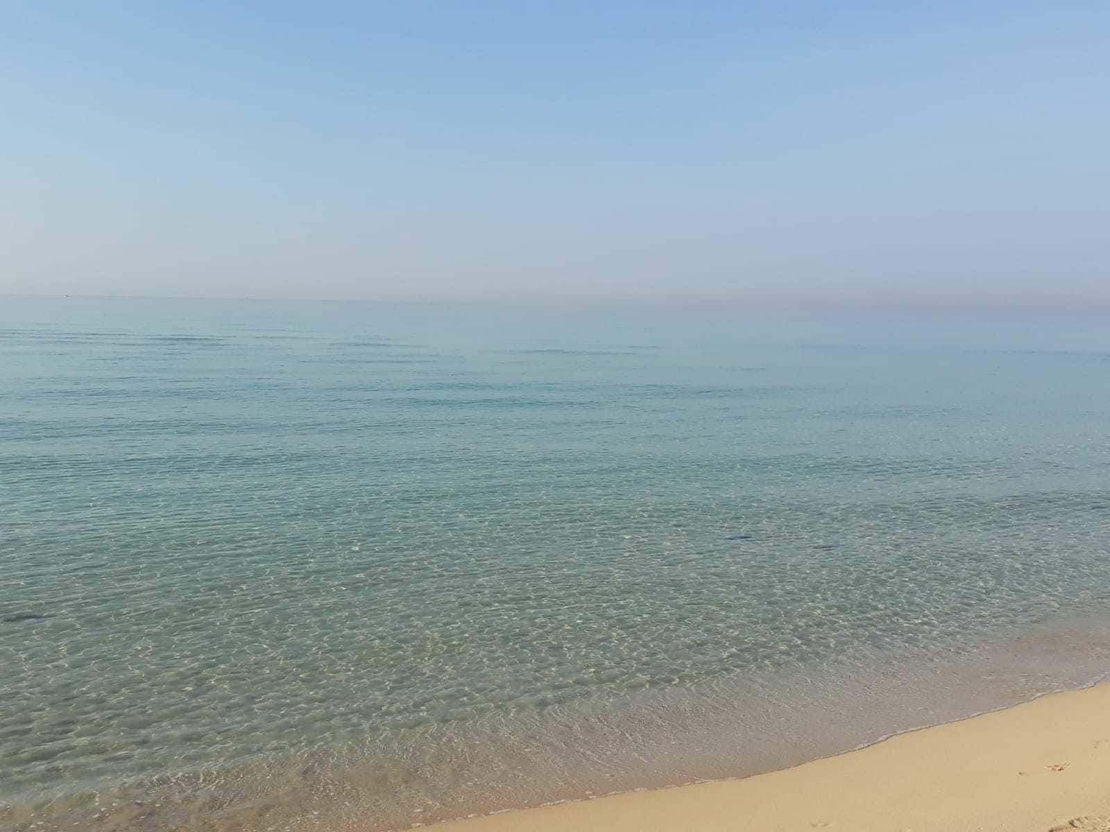 Uma praia com águas cristalinas e rasa e uma extensa faixa de areia.