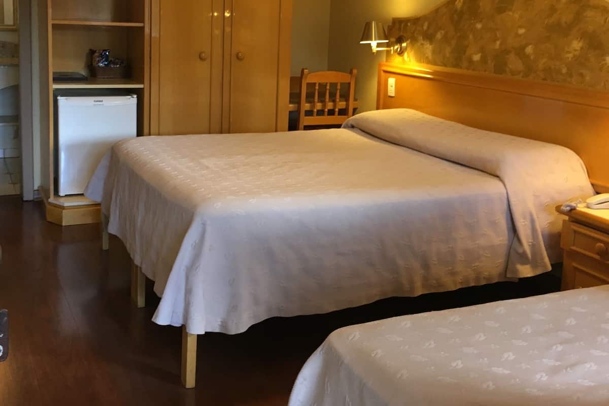 Quarto de hotel com duas camas, um guarda-roupa, uma escrivaninha com luminária e um ventilador de teto.