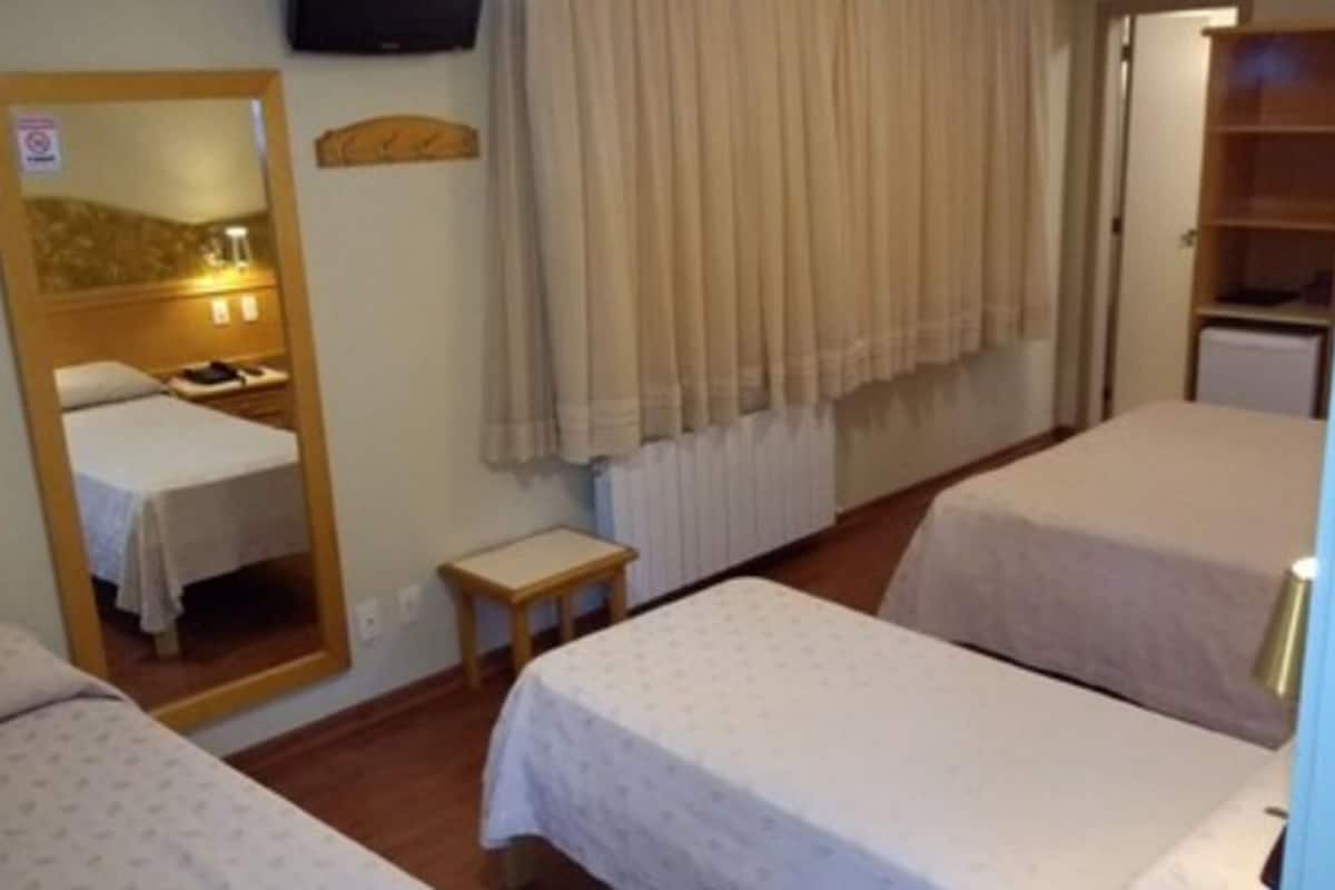 Quarto de hotel com duas camas, uma mesinha, um espelho, uma televisão e uma janela com cortinas.