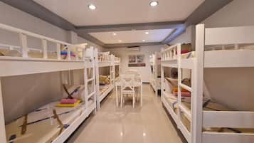 Um dormitório com beliches, uma mesa, cadeiras e um ventilador de teto.