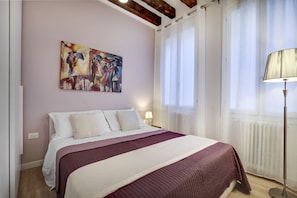 Um quarto com uma cama, um quadro, uma luminária e uma janela com cortinas.