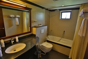 Uma casa de banho moderna com uma pia, sanita e banheira. Há uma janela sobre a banheira, e toalhas estão arrumadas num porta-toalhas.