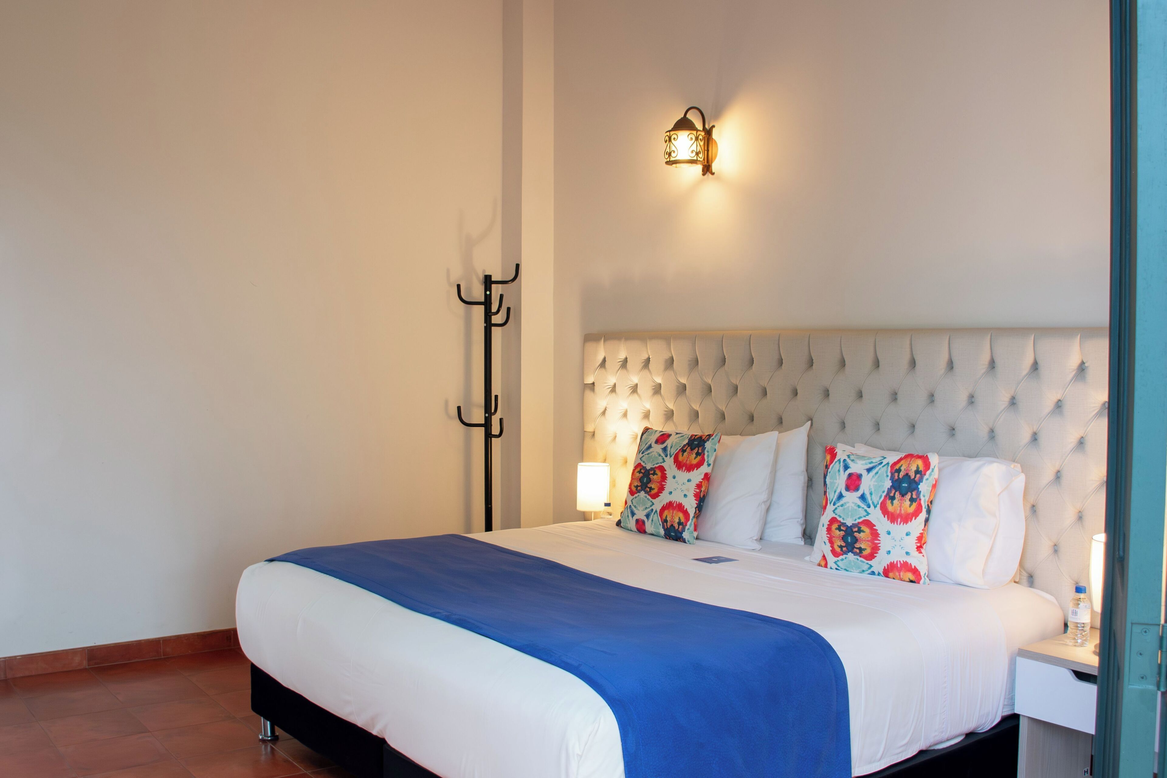 Cama bem arrumada com edredom azul e branco, cabeceira estofada e almofadas decorativas.