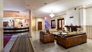 Um saguão de hotel com balcão de recepção, sofás, lareira e escada.