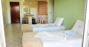 Quarto de hotel com duas camas, uma kitchenette e um espaço de refeições com banquetas.