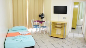Quarto de hotel com cama, escrivaninha com cadeira, ventoinha e televisão na parede.