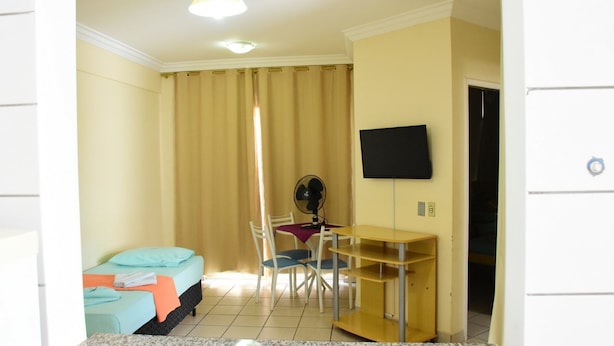 Quarto de hotel com cama, secretária com cadeira, televisão e janela com cortinas.