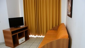 Uma sala de estar com um móvel de madeira para TV, um sofá e uma cortina.