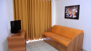 Um quarto com escrivaninha de madeira, monitor preto, sofá laranja, cortina e uma pintura abstrata pendurada na parede.