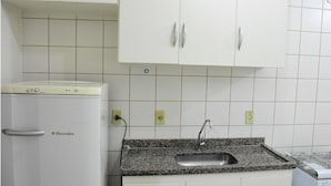 Cozinha com armários brancos, bancada de granito, pia, fogão e geladeira.