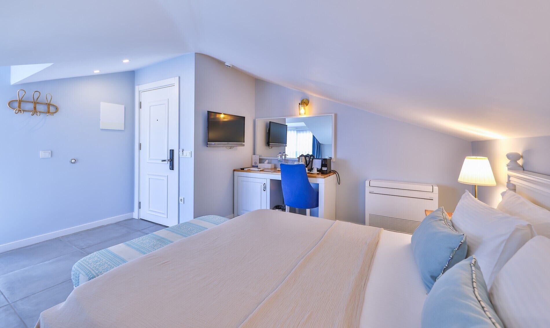 Quarto de hotel moderno com cama, escrivaninha, cadeira, televisão e um pequeno aquecedor.
