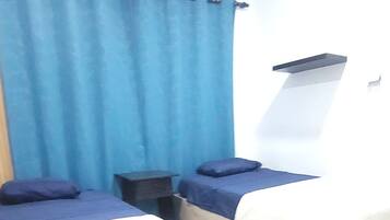 Quarto de hotel com duas camas, uma mesinha, ar-condicionado na parede e uma janela com cortinas.