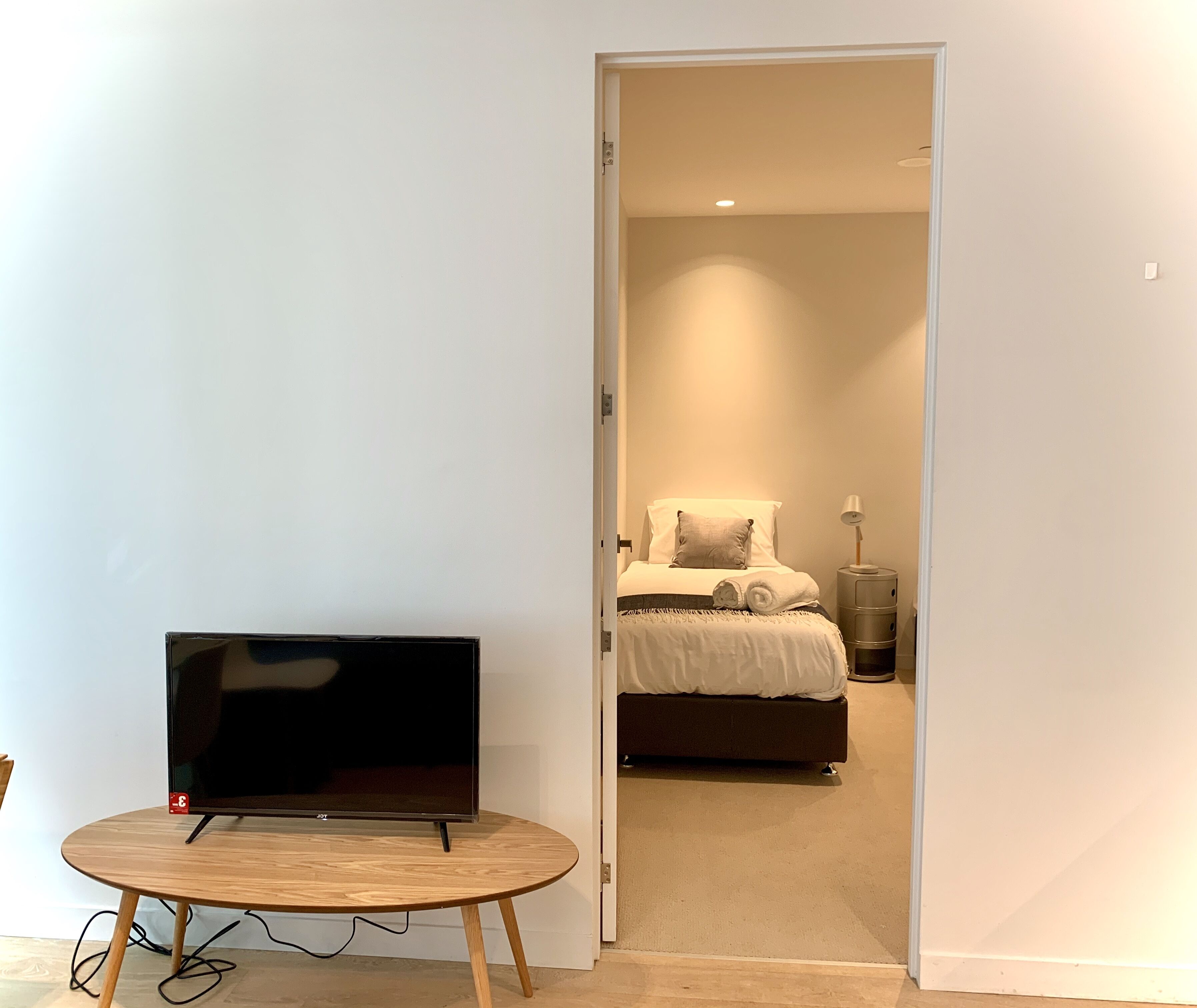Quarto com cama, luminária de cabeceira e televisão sobre uma mesa de madeira.