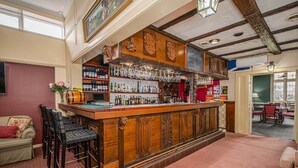 Uma área de bar com balcão de madeira, prateleiras com garrafas e banquetas.