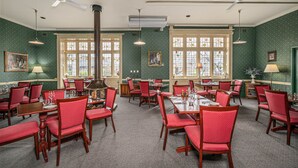 Uma sala de jantar com várias mesas e cadeiras, ventiladores de teto e grandes janelas com painéis de vidro decorativos.