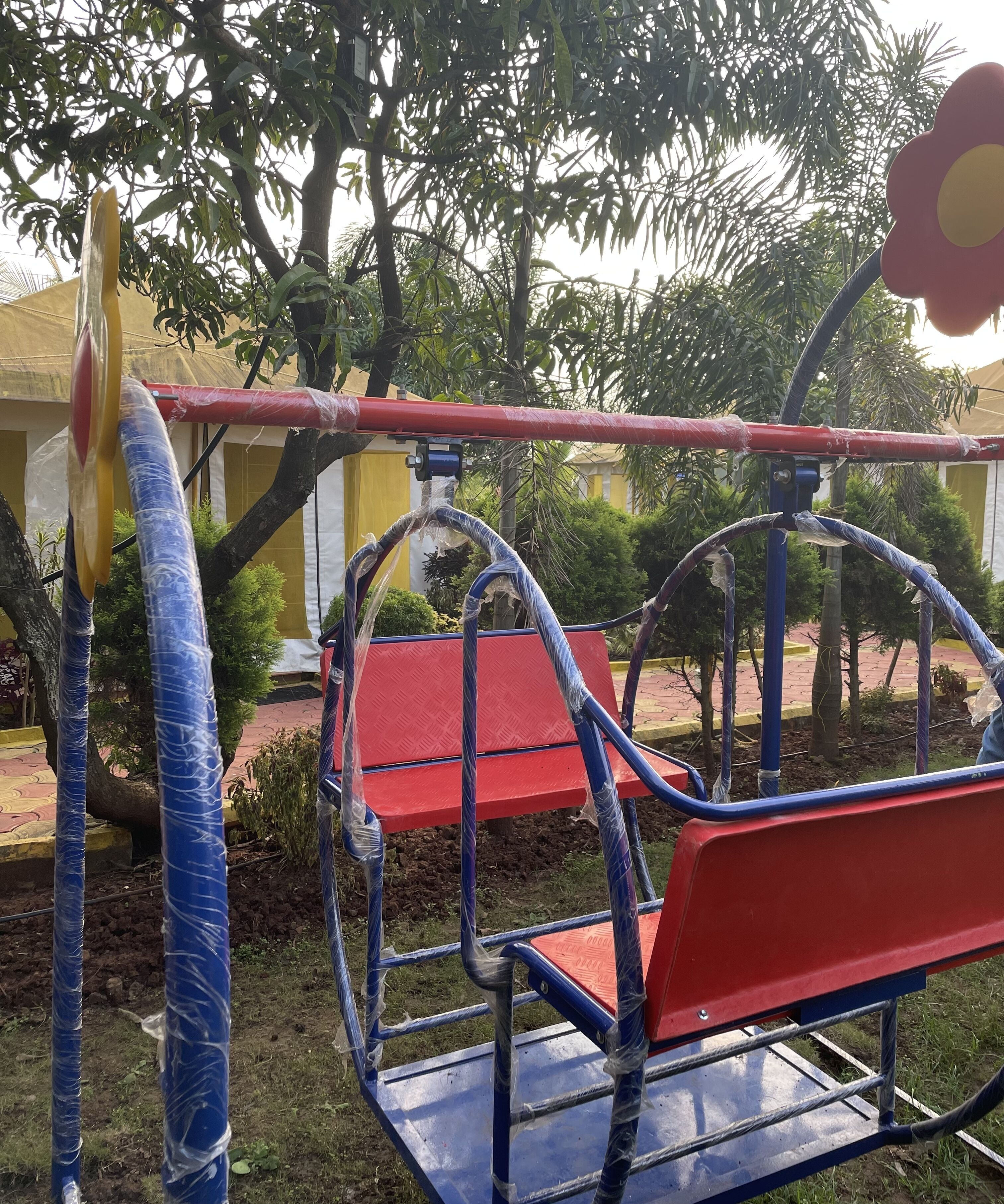 Um parquinho com balanço e escorrega, cercado por árvores e um prédio ao fundo.