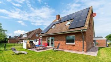 Uma casa com painéis solares no telhado, fachada de tijolos e gramado bem cuidado com mobiliário de exterior.