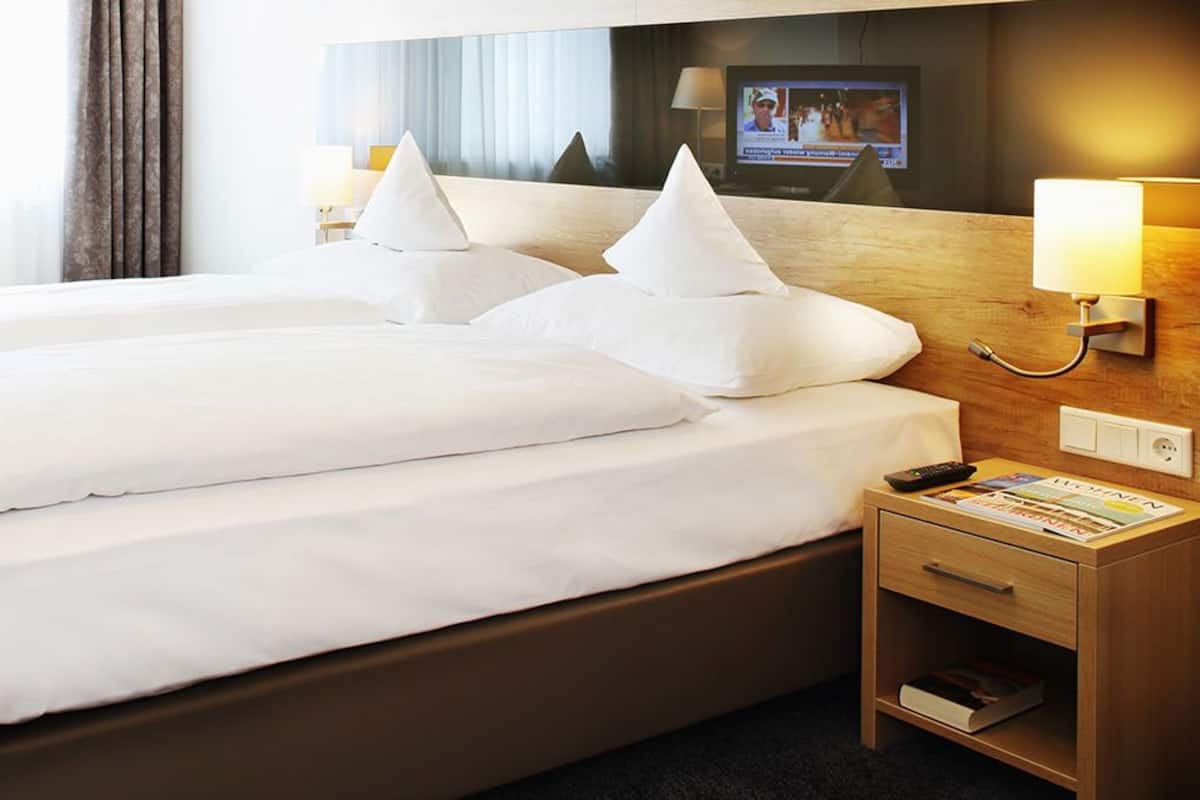 Quarto de hotel com uma cama grande, duas mesas de cabeceira, uma TV e um abajur.