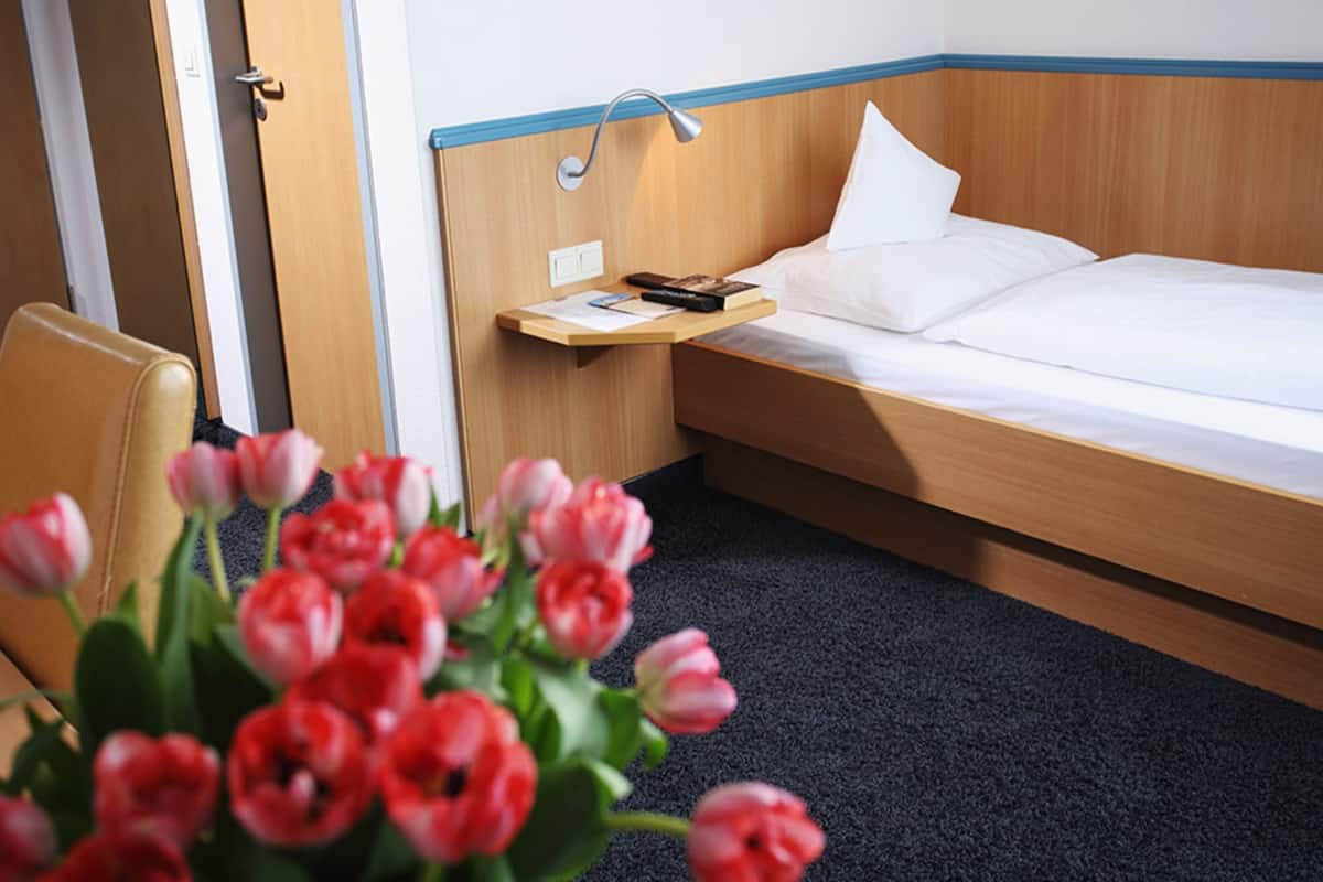 Quarto de hotel com cama, mesa de cabeceira, escrivaninha e cadeira.