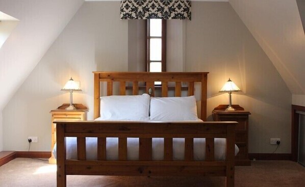 Um quarto com cama de madeira, duas luminárias de cabeceira, uma janela e cortina estampada.