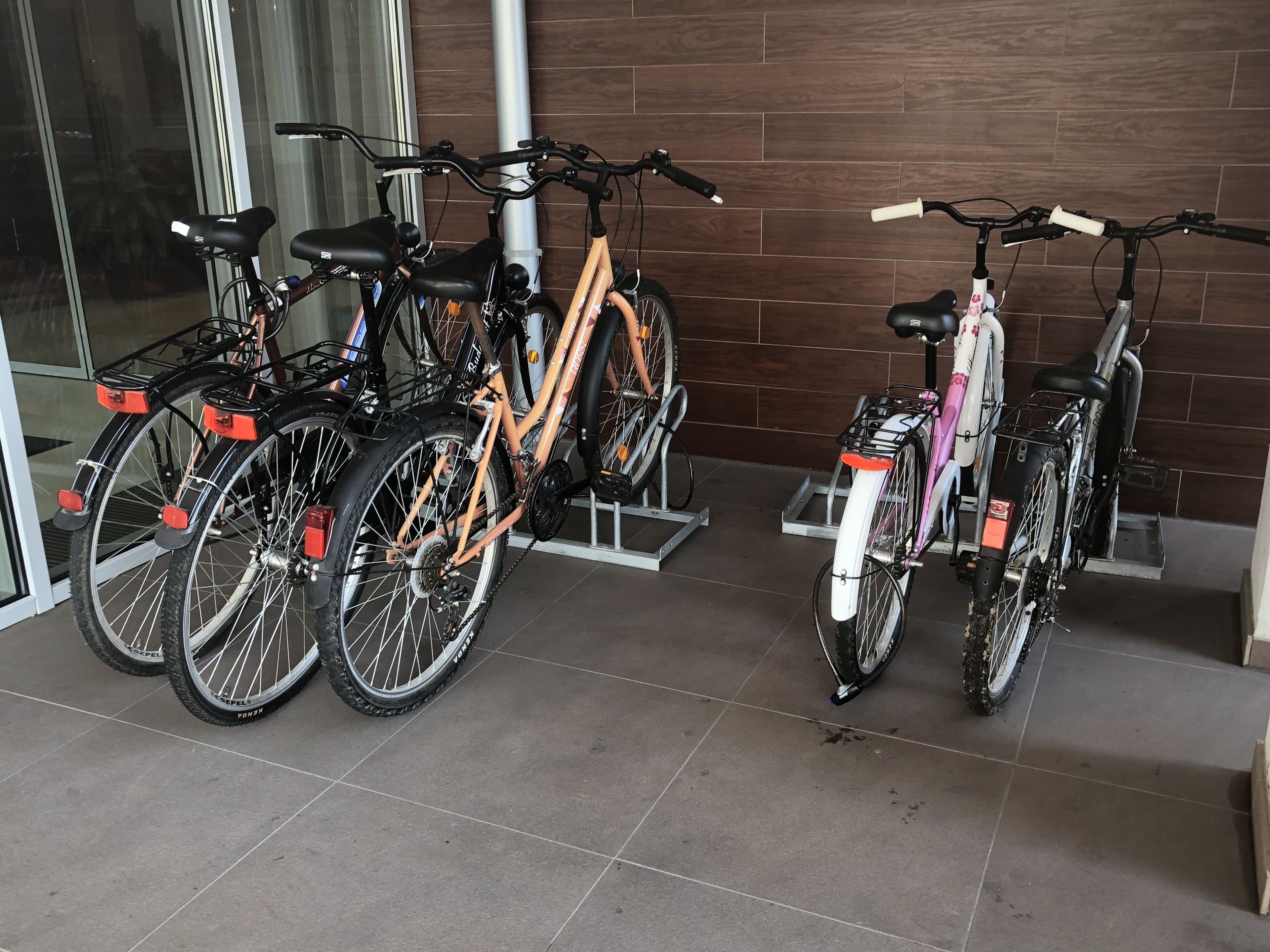Bicicletas estacionadas em ambiente interno com piso de azulejos e parede de madeira.