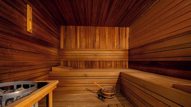 Uma sauna de madeira com bancos, um banco de pedra e um balde com um remo.