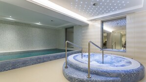 Uma piscina interior moderna com hidromassagem, azulejos e divisória de vidro.