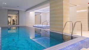 Piscina interior moderna com água cristalina, fundo de vidro e grades de metal.