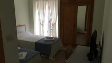 Quarto de hotel com duas camas, uma escrivaninha, uma cadeira, uma televisão e um guarda-roupa.