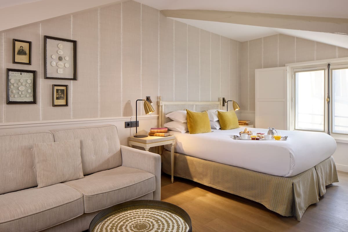 Quarto de hotel com cama, um sofá, mesa de cabeceira e janela.