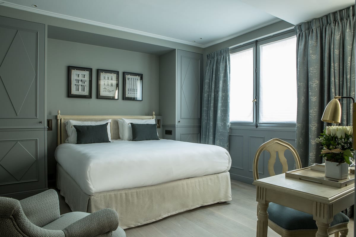 Quarto com uma cama grande, uma cadeira, uma mesa e uma janela com cortinas.