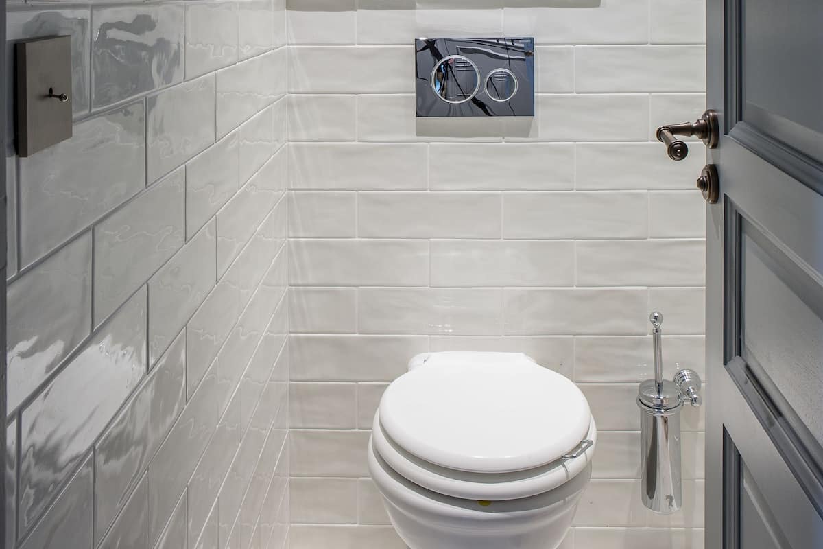 Casa de banho com azulejos brancos, sanita, bidé e dois quadros com gravuras botânicas na parede.