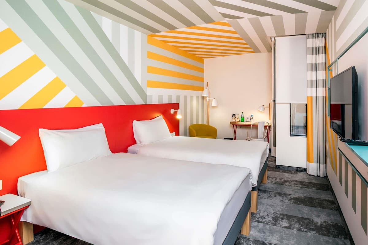 Quarto de hotel com duas camas, uma mesa, uma cadeira, uma televisão e teto listrado.