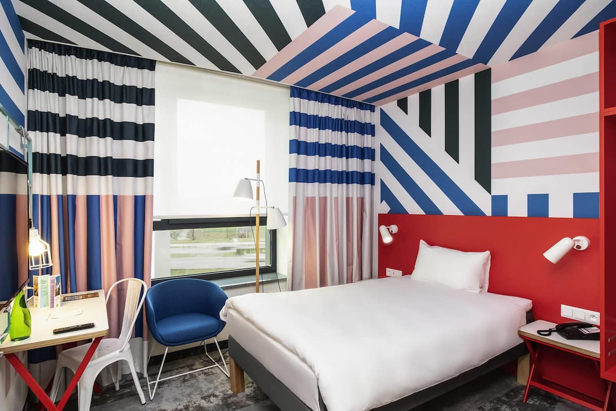 Quarto de hotel com cama, secretária, cadeira e vista para o exterior.