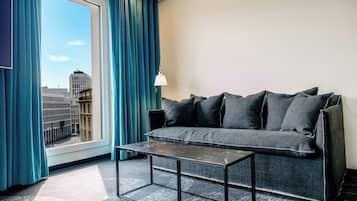 Quarto moderno com sofá, mesinha e vista para a paisagem urbana através de uma grande janela.