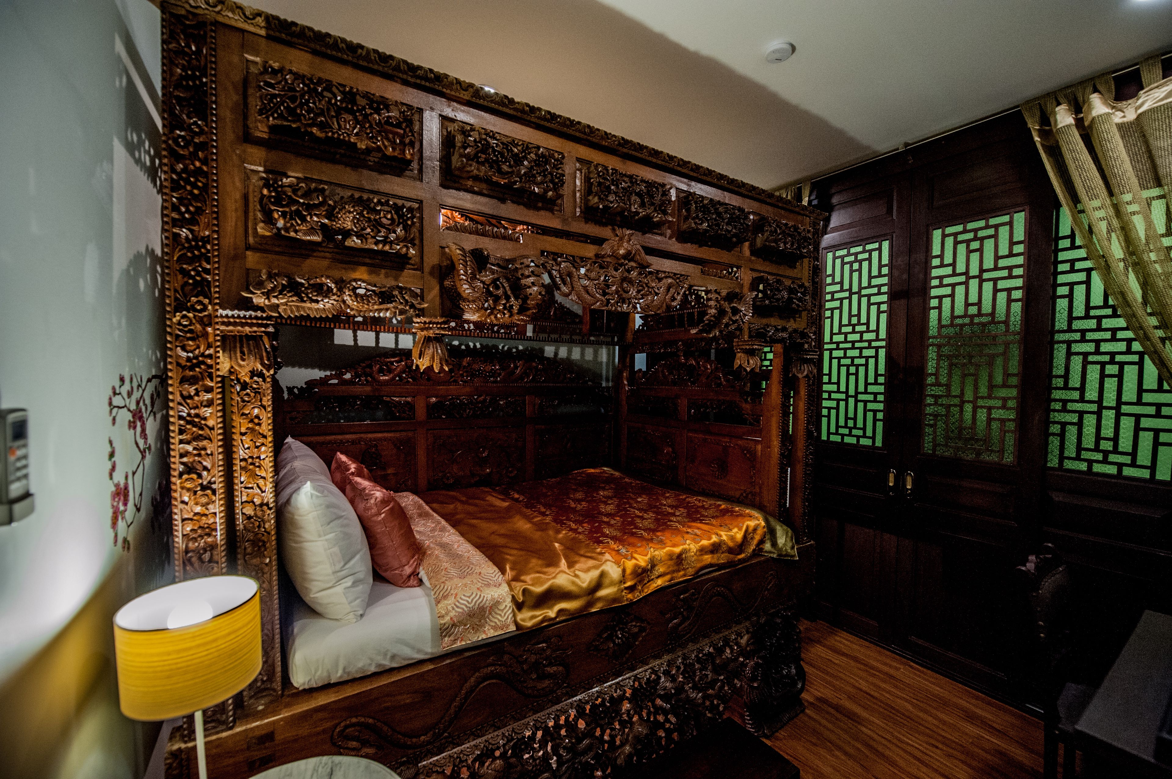 Quarto tradicional com cabeceira de madeira, cama com colcha dourada e porta verde estampada.