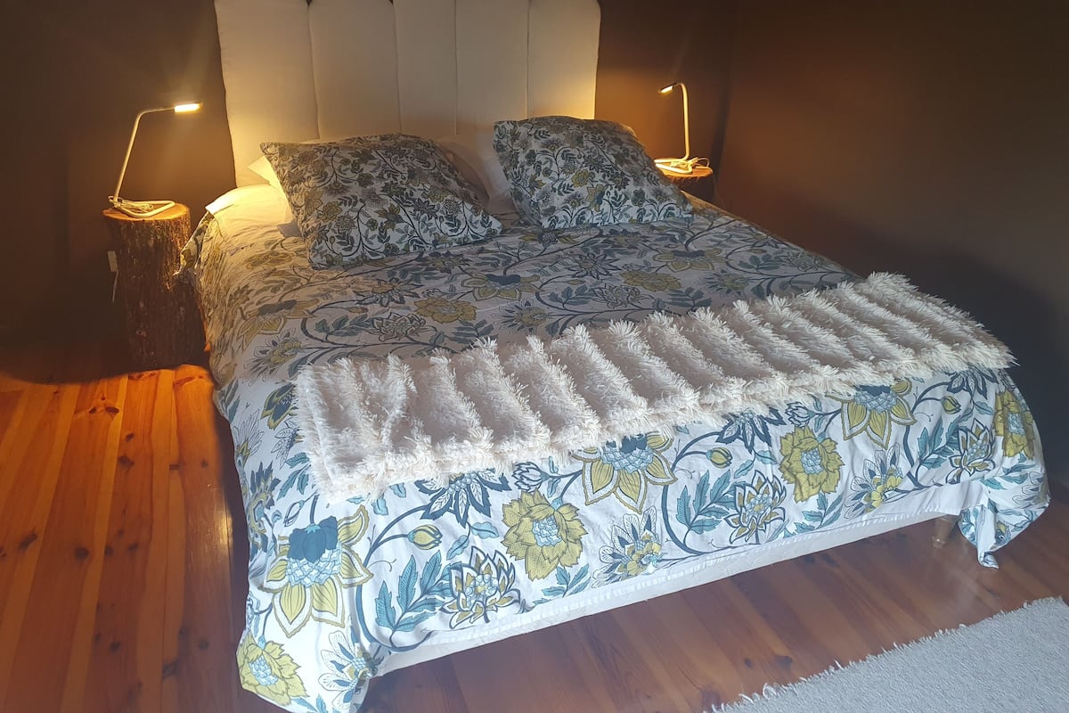 Uma cama com colcha florida, duas almofadas e duas luminárias de cabeceira.