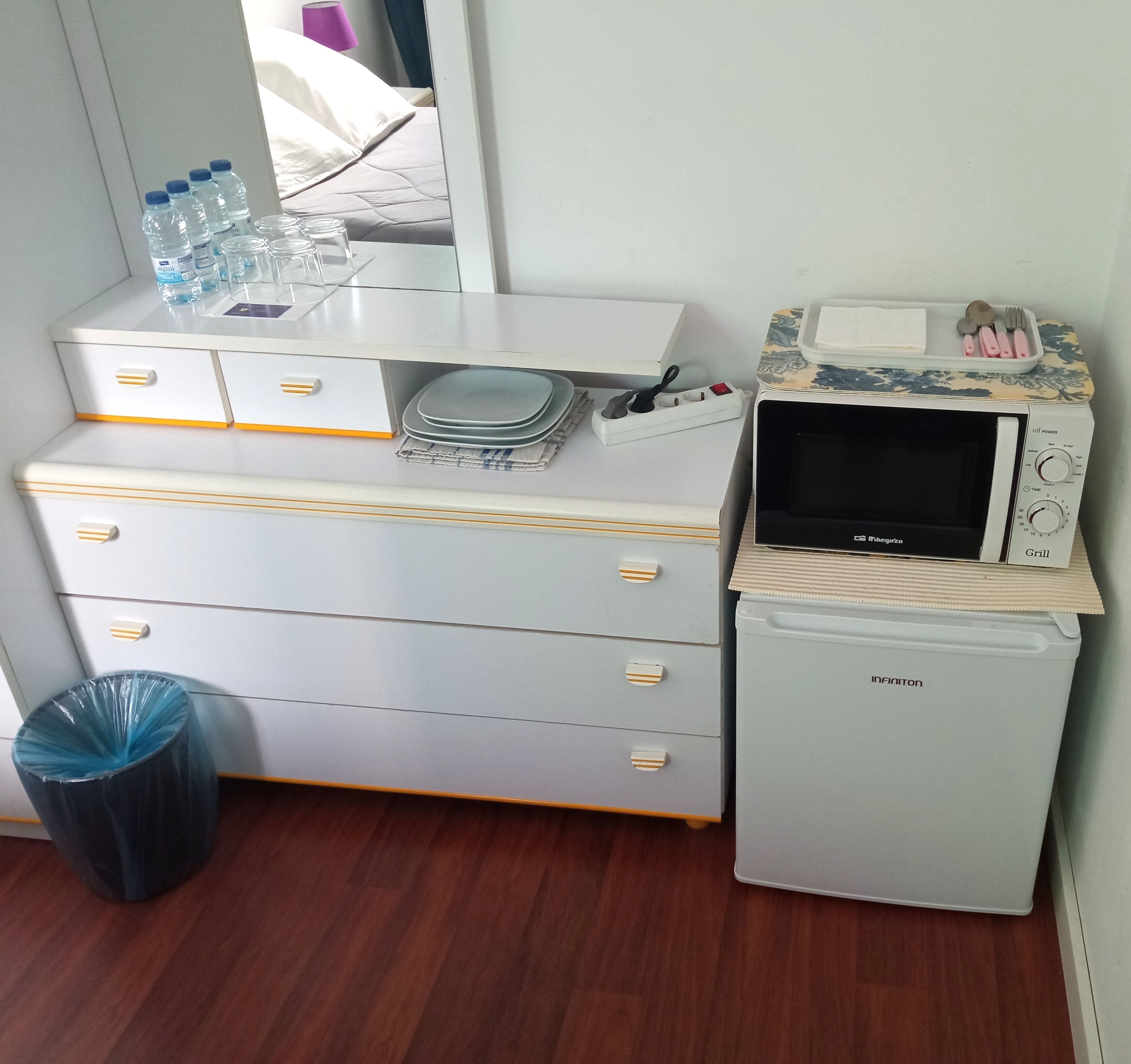 Uma cozinha compacta com micro-ondas, mini geladeira e bancada com garrafas de água e copos.