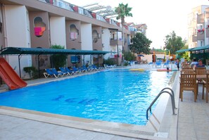 Piscina com água azul, cercada por espreguiçadeiras e um escorregador.