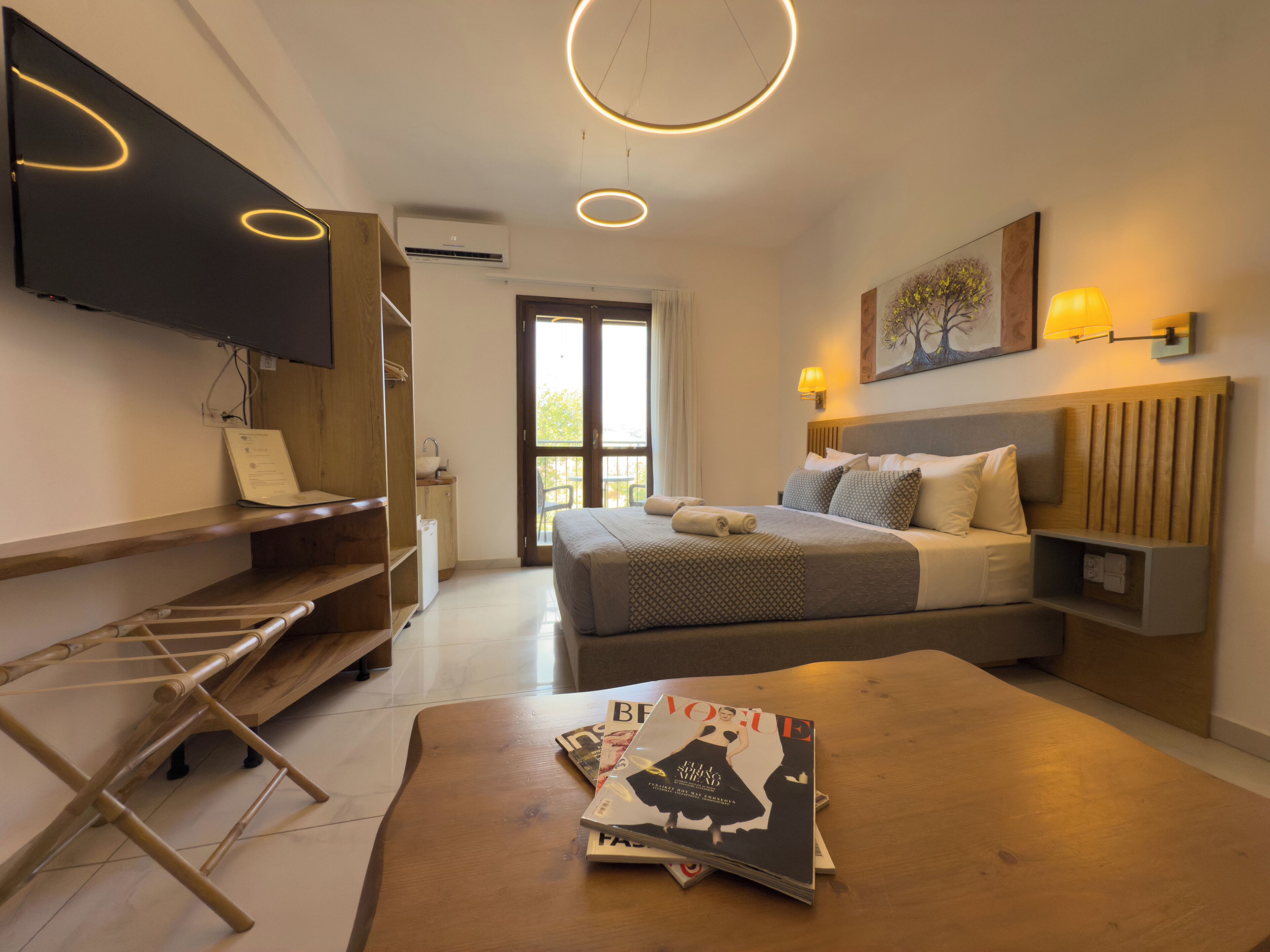 Quarto de hotel moderno com cama, mesas de cabeceira, televisão e escrivaninha de madeira.
